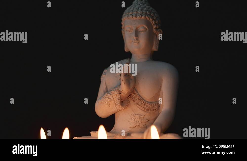 Rotating sitting Buddha statue candle light against black background ...