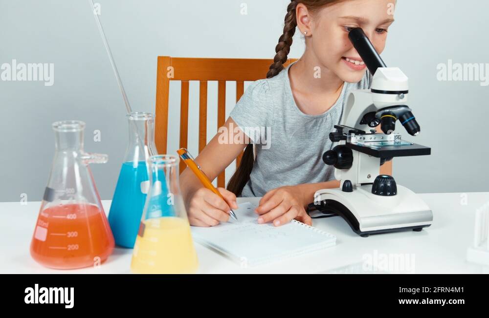 School girl using microscope and something writing in her exercisebook ...