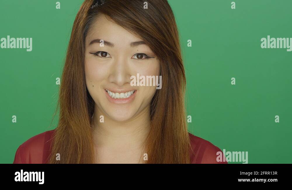 Young Asian woman awkwardly smiling, on a green screen background Stock ...