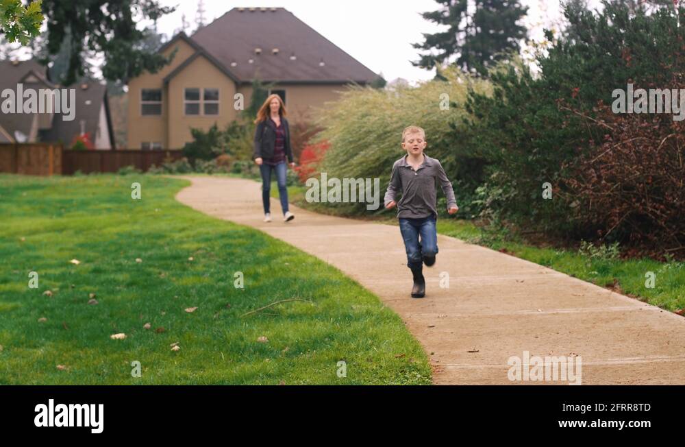Little boy running down a path at a park while his mother follows Stock ...