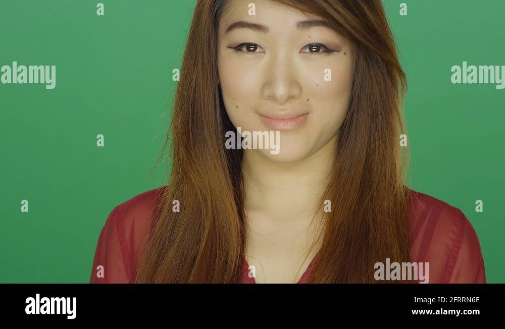 Young Asian woman awkwardly smiling, on a green screen background Stock ...