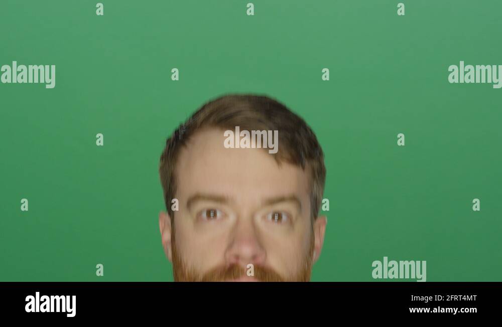 bearded man smiles and makes silly faces, on a green screen background ...