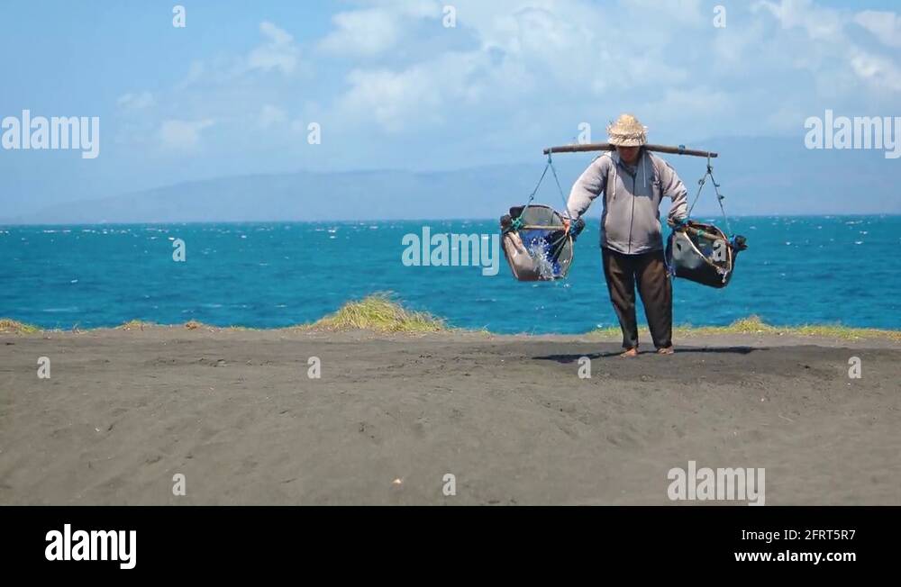 Woman sloshing sea water over sand from shoulder mounted buckets to ...