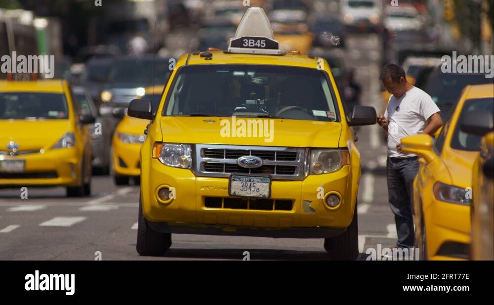 Taxi driver checking his phone next to parked cab on busy New York City ...