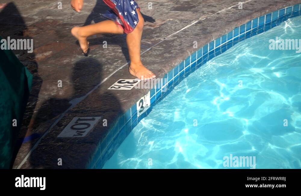 A boy doing a cannonball and jumping into a pool at a hotel resort ...