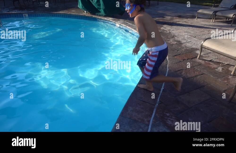 A boy doing a cannonball and jumping into a pool at a hotel resort ...