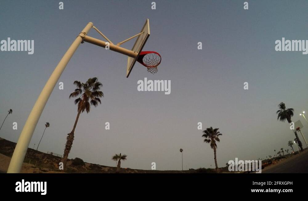 A young man shooting hoops on a basketball court at the beach as the ...
