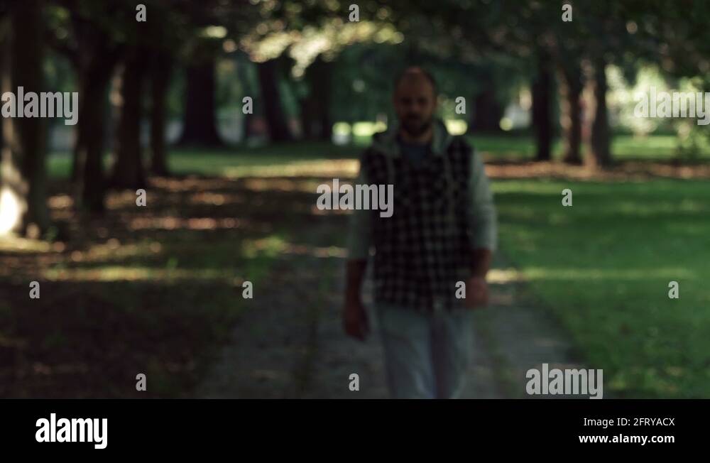 bald man walking in the park at the camera, stop crosses his arms and ...
