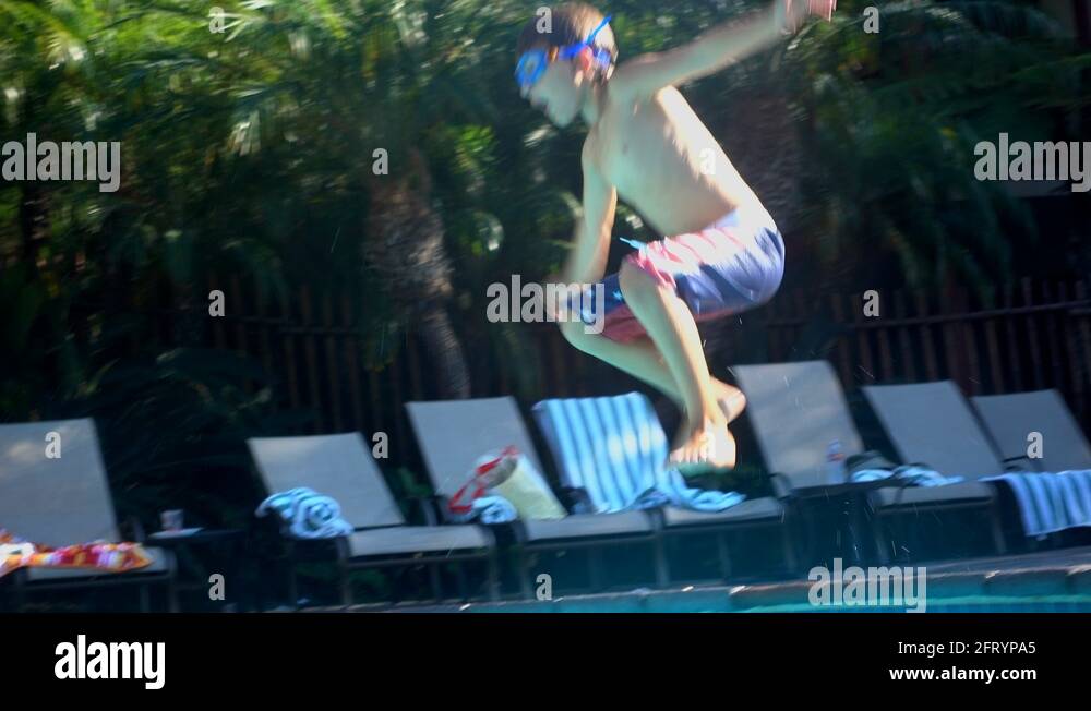 A boy doing a cannonball and jumping into a pool at a hotel resort ...