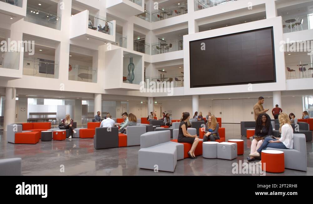 Students sit talking under AV screen in atrium at university Stock ...