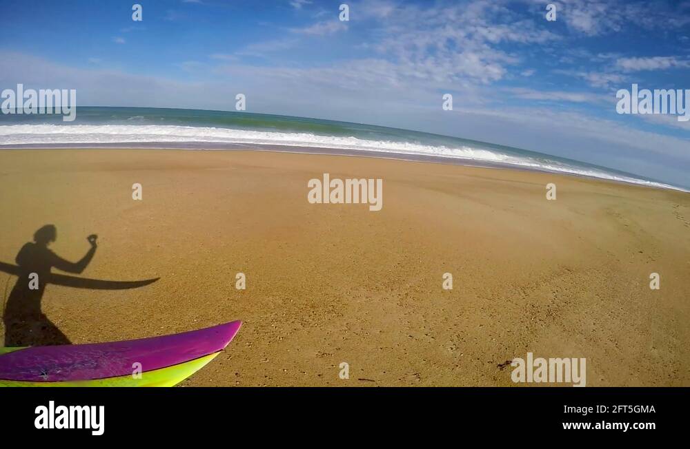 POV of a surfer running on the beach with his surfboard and making a ...