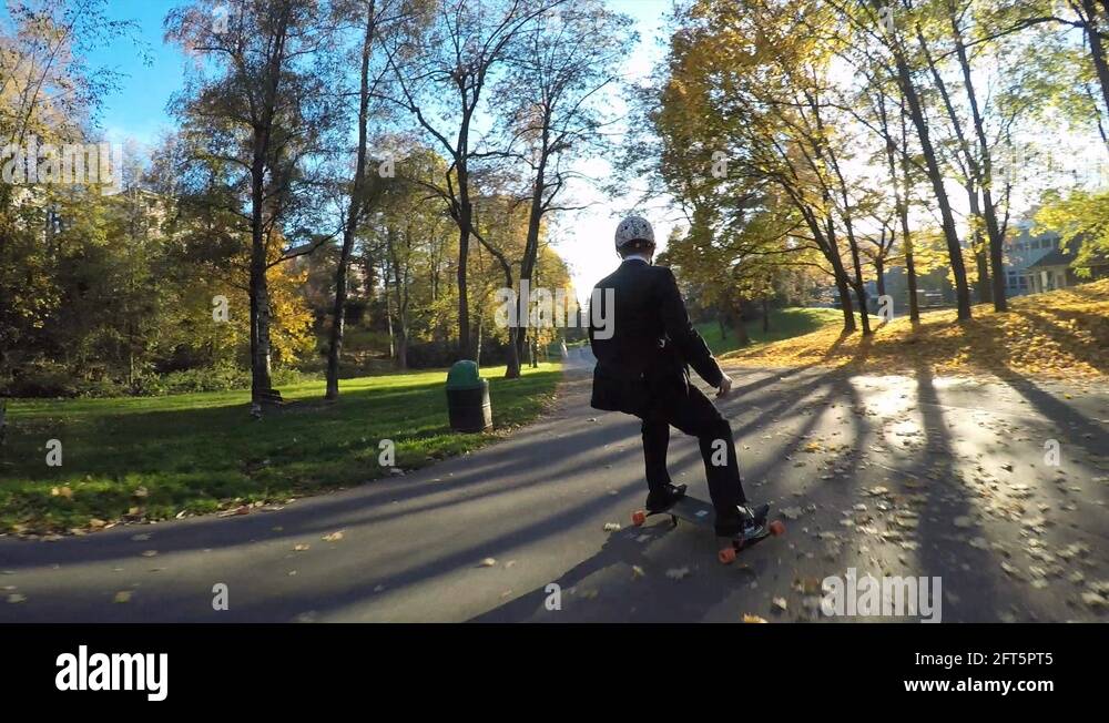 A young man longboard skateboarding downhill in a city park wearing a ...