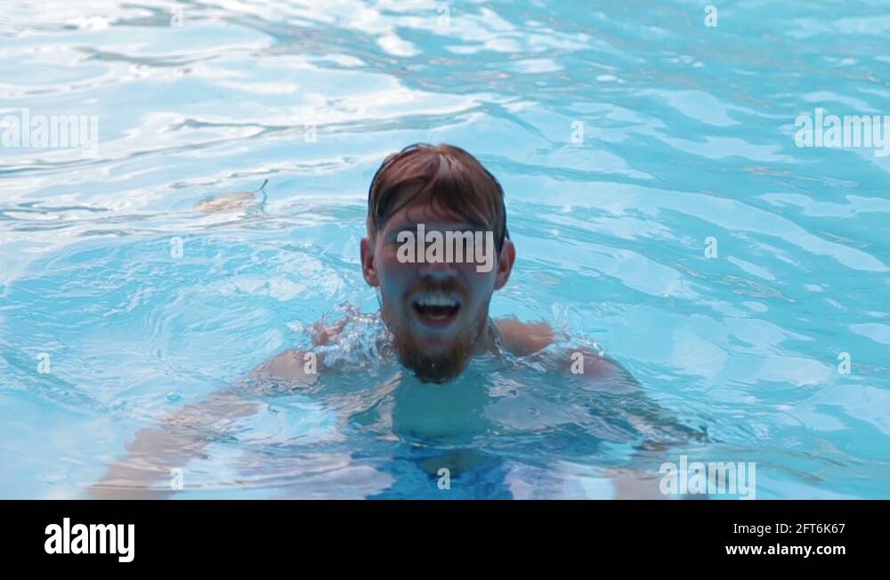 a young man with a beard dives and comes up with a splash in the pool ...