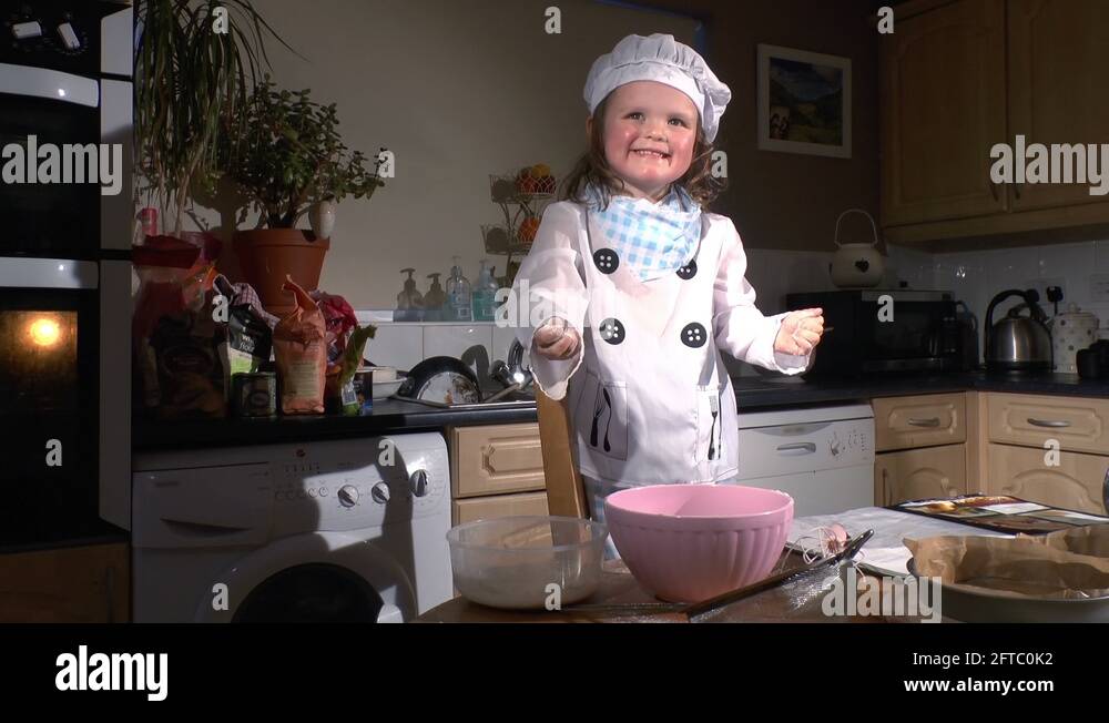Little smiley chef girl throwing flour in a mixing pot filmed in slow ...