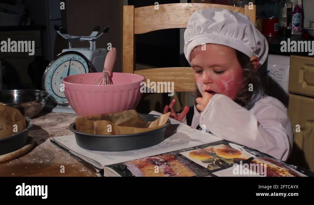 Little messy girl dressed as a chef with flour in her face and hands ...