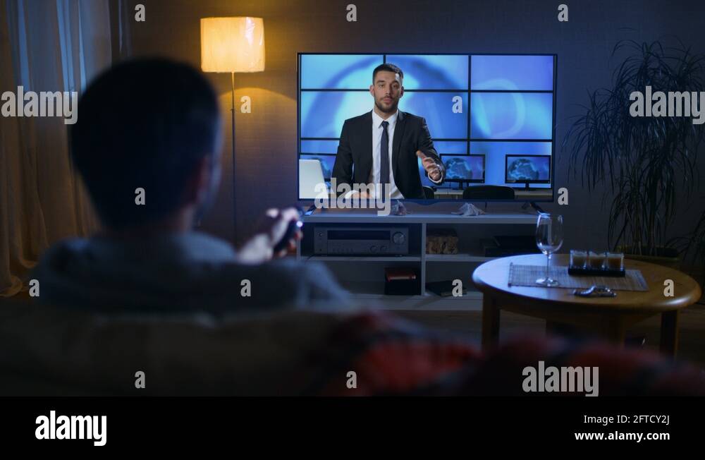 Back View of a Man Sitting on a Couch Watching Breaking News on TV ...