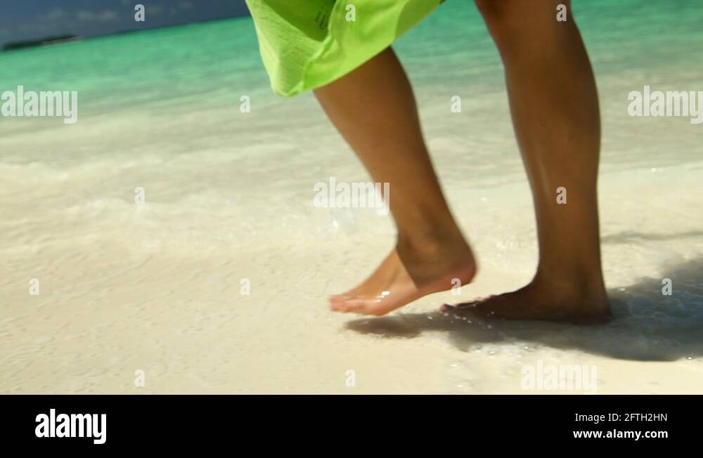 A woman wearing a sarong walks on the beach at a tropical island resort ...