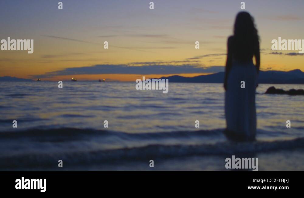 Long back view shot of woman standing and looking at the beach. The ...