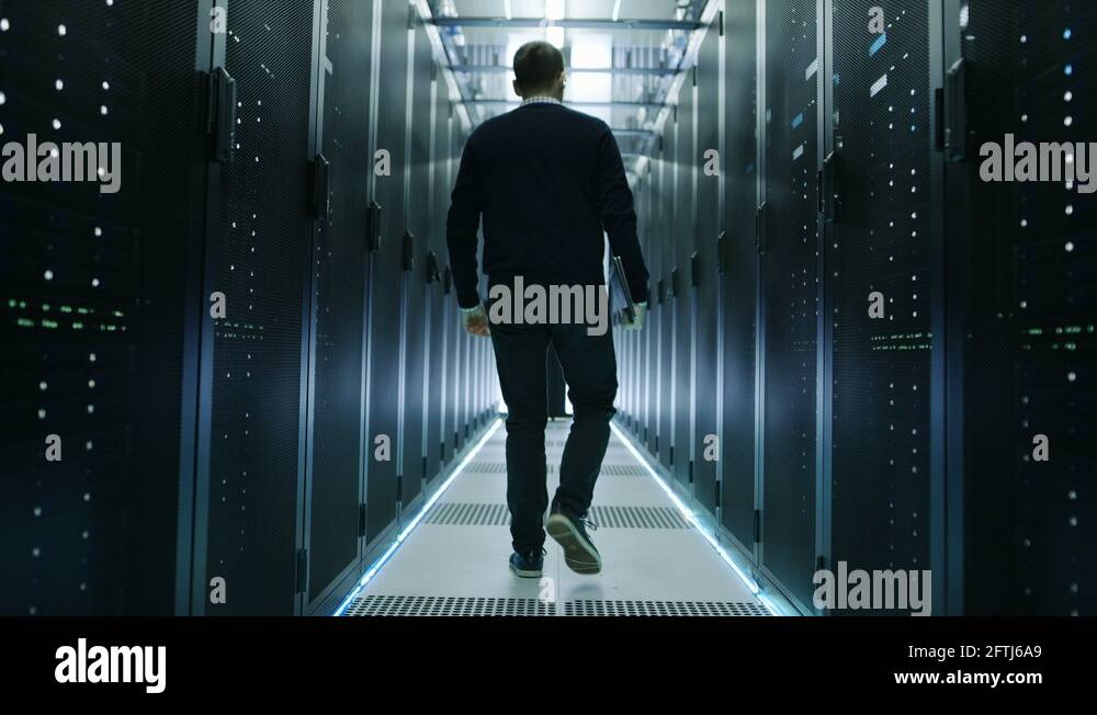 Back View of IT Engineer Walking Through Data Center with Working Rack ...