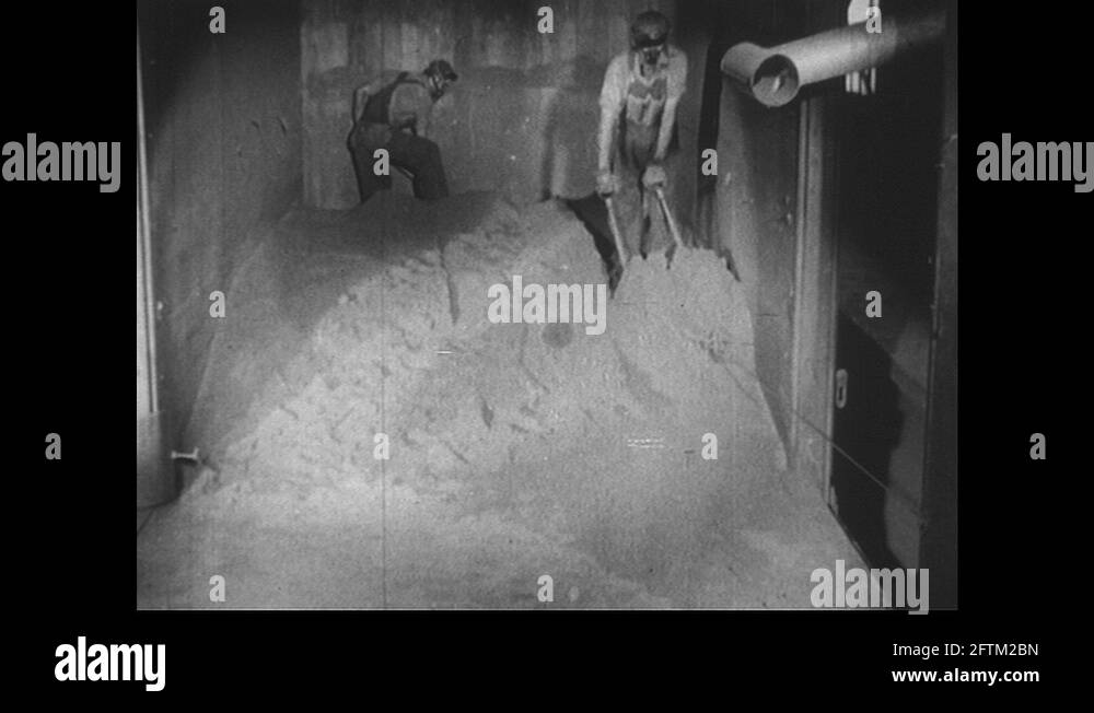 1940s: Two men load wheelbarrow with grain inside train carriage ...