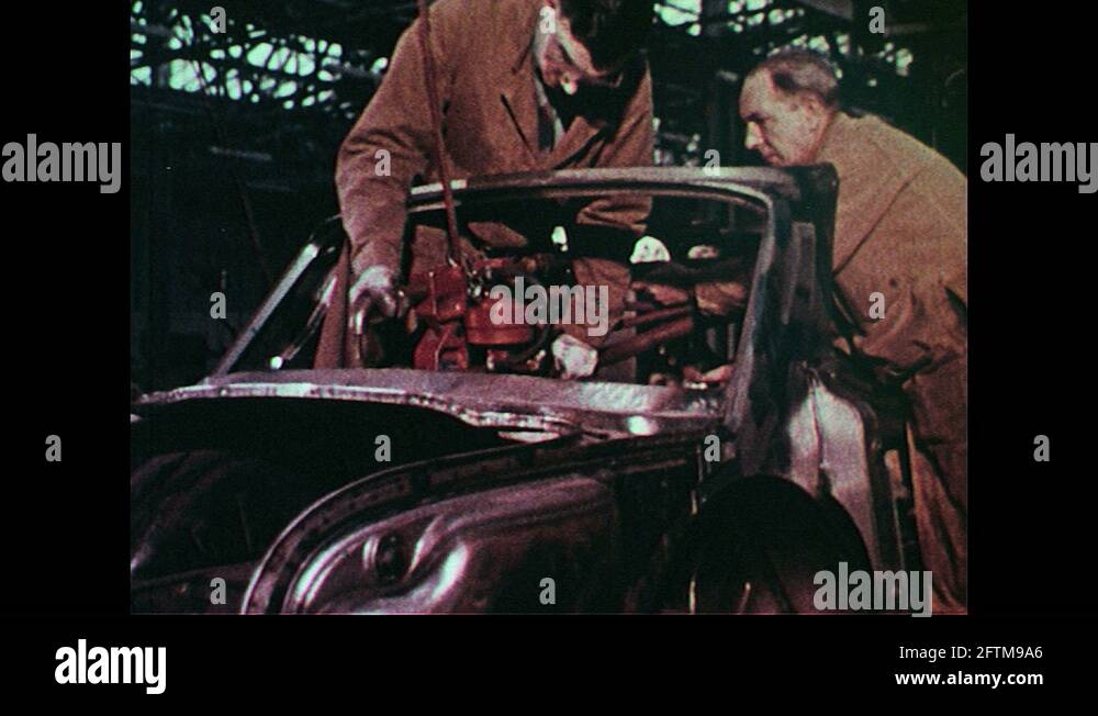 1960s: Engineers in factory build new car. Man carries car part across ...
