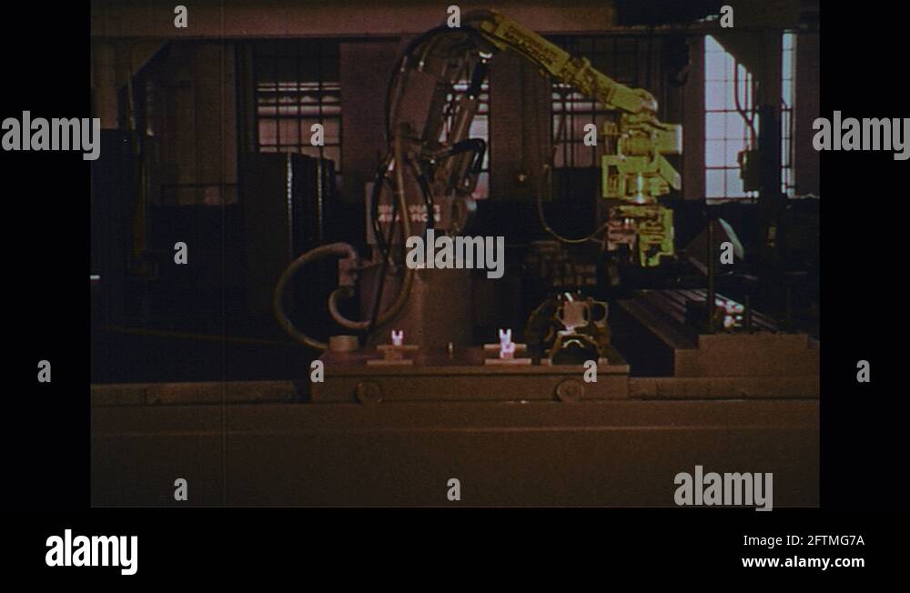 1980s: industrial robotic arm in factory picks up car engine part and ...