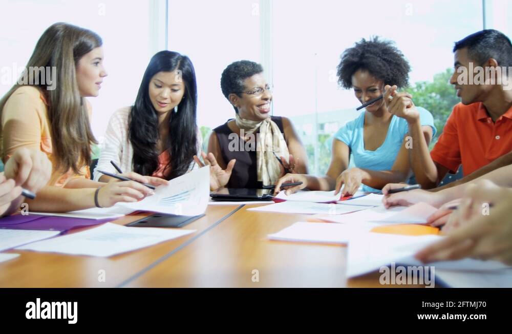 Young multi ethnic male and female teenagers sitting around table with ...
