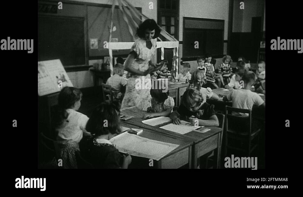 1950s. Teacher in classroom with students drawing, writing, and reading ...