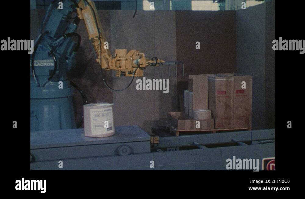 1980s: Long shot of industrial robotic arm in a factory carries ...