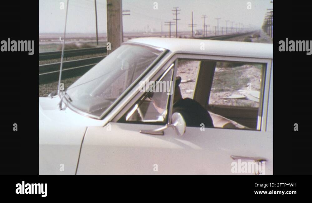 UNITED STATES: 1970s: car driver looks both ways at railway crossing ...