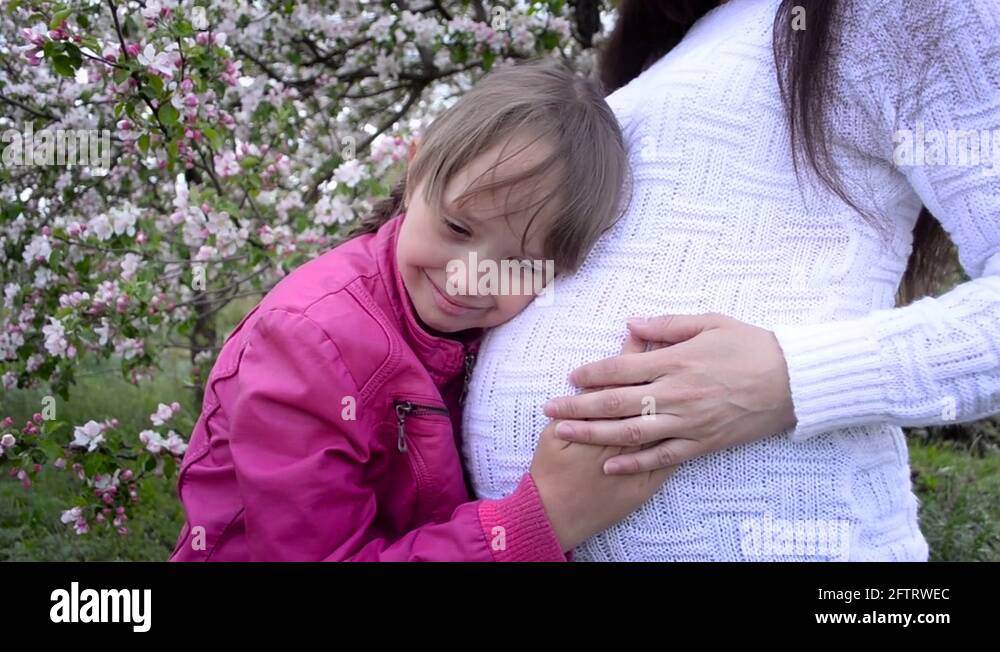 Young girl smiling hugs belly of pregnant mother. Pregnant mother ...
