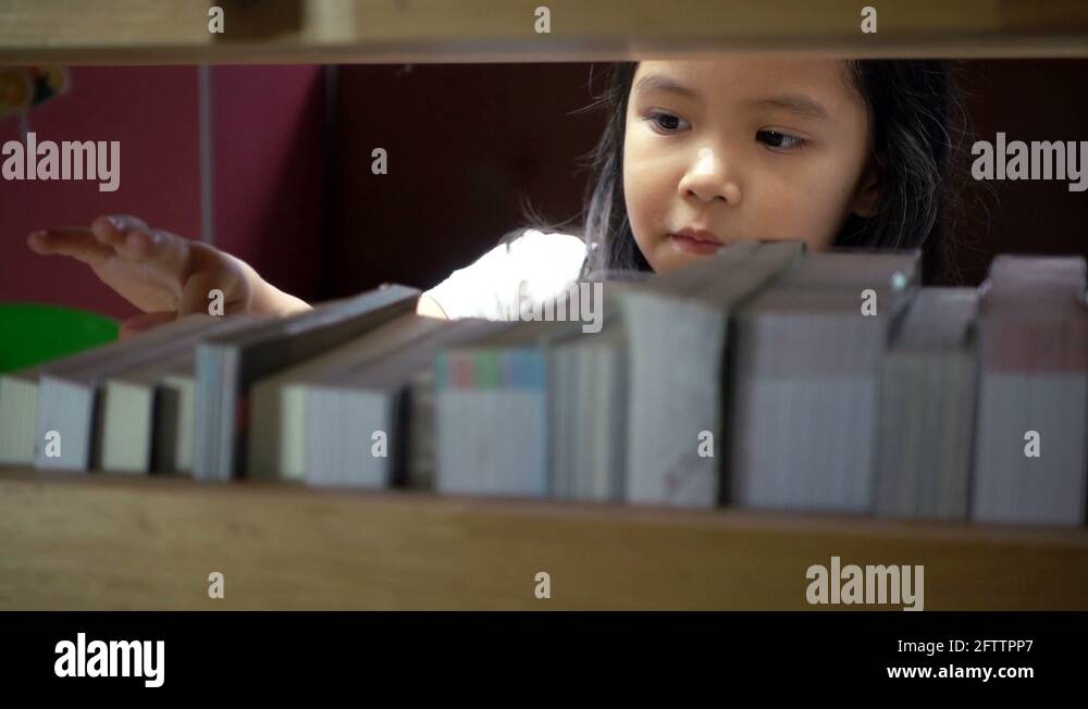 Cute asian little girl is finding a book on bookshelf in the library ...