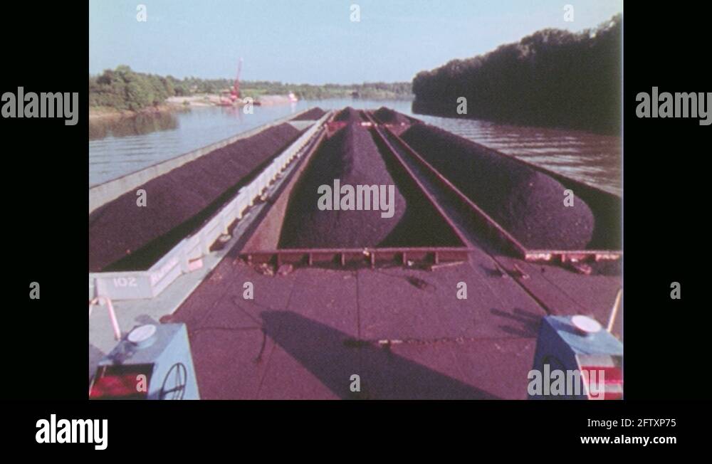 1970s: barges of coal float down river. man in boat cockpit steers ...