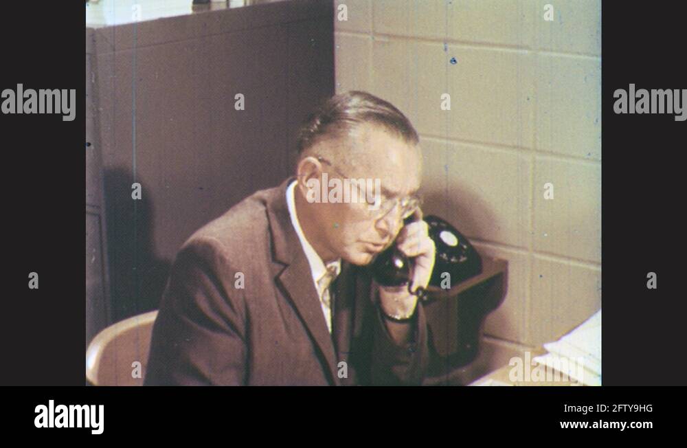 1960s: UNITED STATES: man speaks on telephone from desk. Man nods head ...