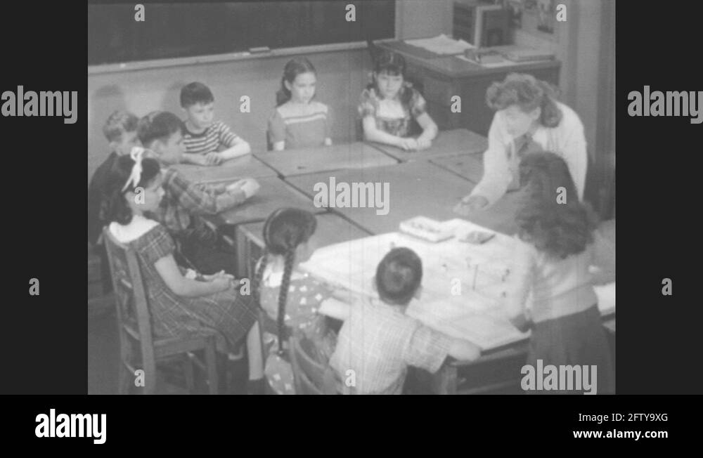 1940s: Teacher and students look at map on table in classroom. Students ...