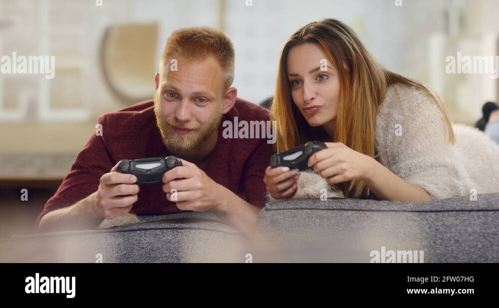 Playful cute couple falling off couch while playing video games Stock ...