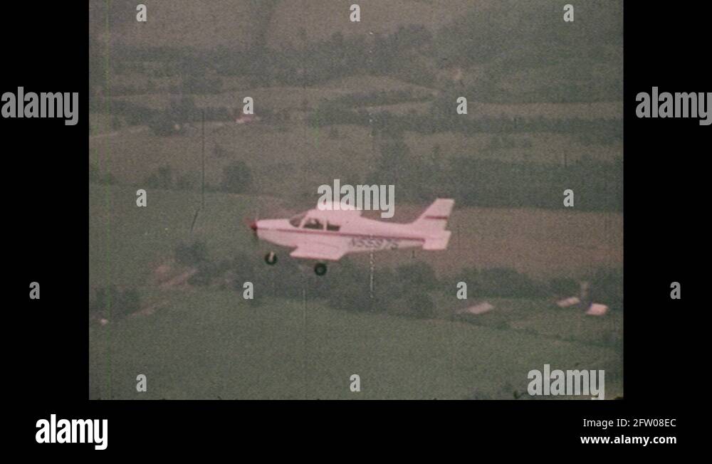 1970s: UNITED STATES: plane flies in sky over fields. Girl has flying ...