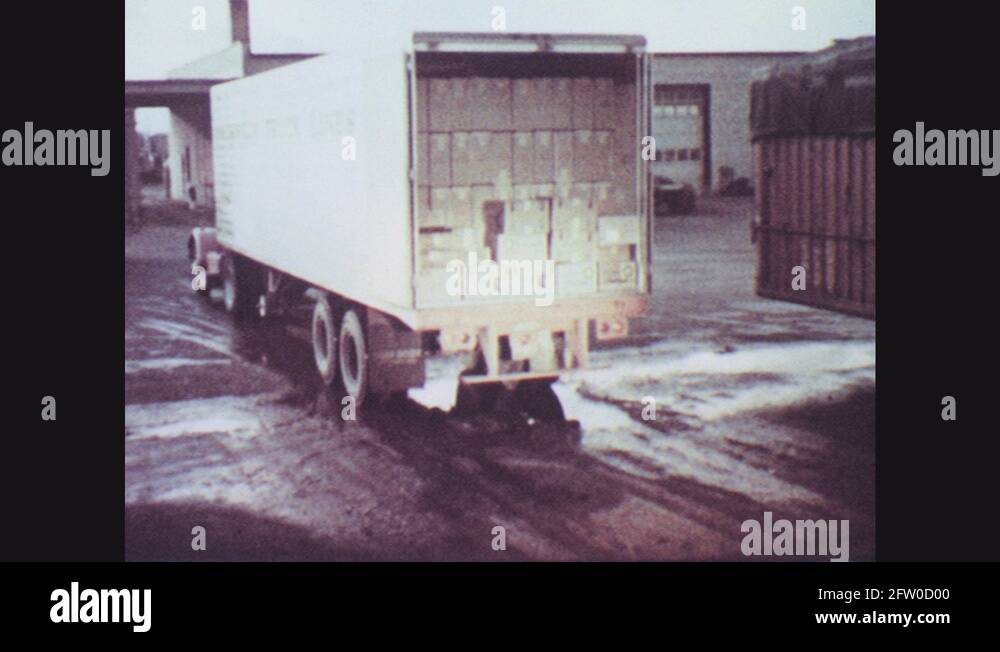1950s: Truck full of boxes backs up to loading dock. Two men on dock ...