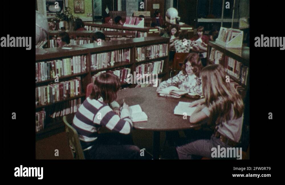 1970s: UNITED STATES: students work in group in library. Girl flicks ...