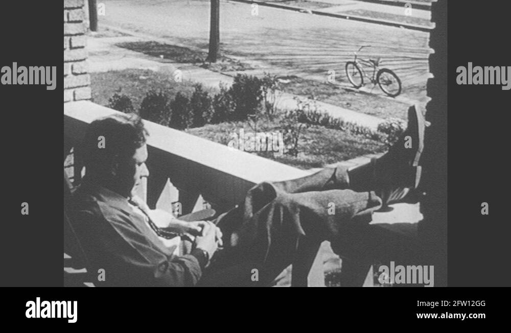 1940s: Man dozes with feet up on porch. Boy on bike throws newspaper ...