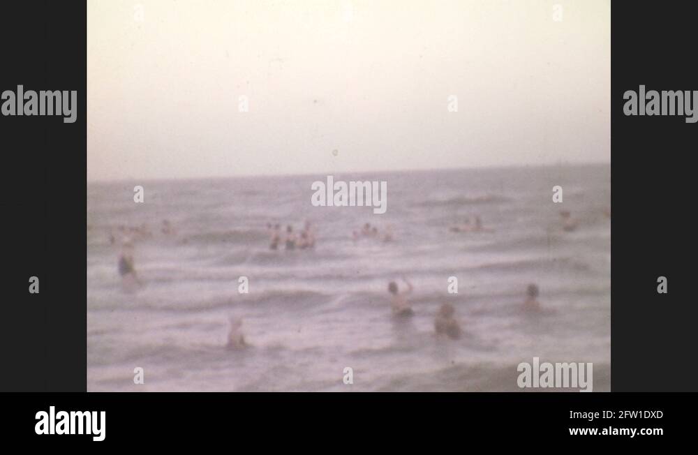1930s: A crowd of people wade, swim and play in the waves at a beach ...
