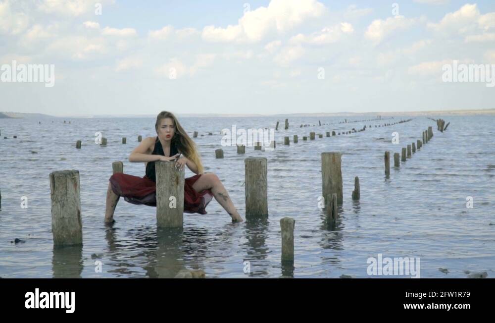 Blonde with long hair in a red dress in the mud beautifully posing in ...