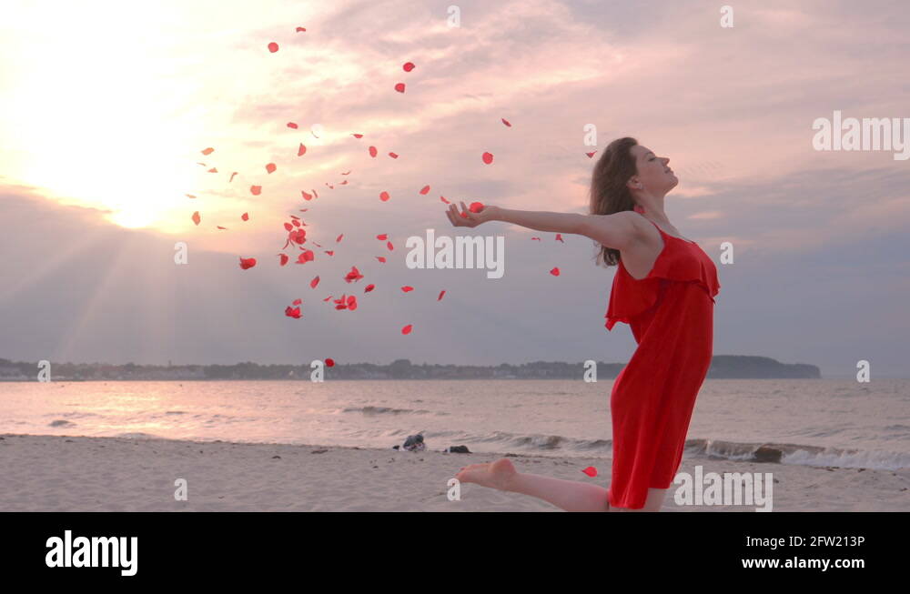 Beautiful woman in red dress throwing rose petals on sea background ...