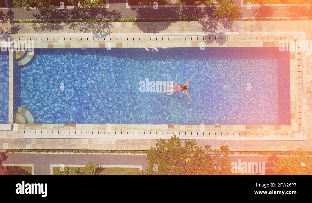 AERIAL TOP DOWN LENS FLARE: Woman in pink bikini swimming in refreshing ...
