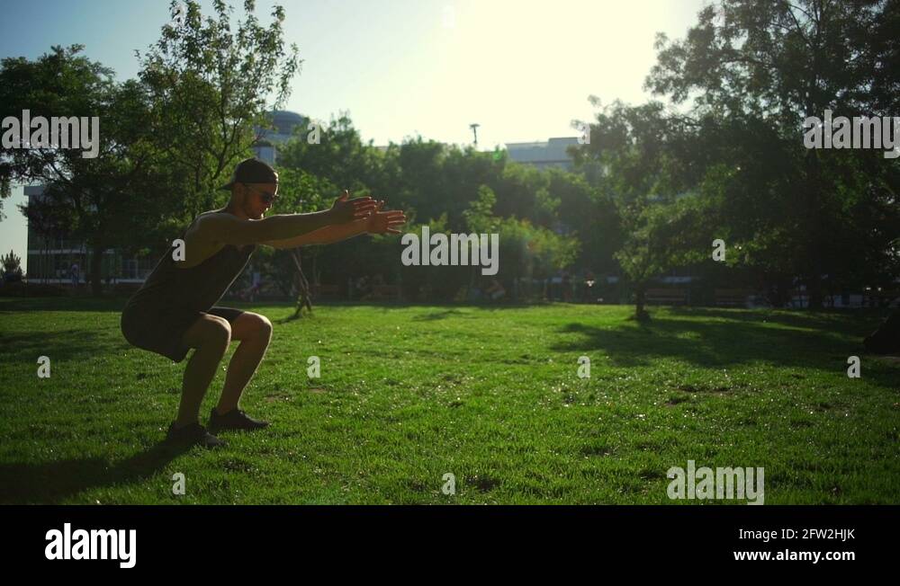 Strong man do static squat exercises on sunny green meadow rapid slow ...
