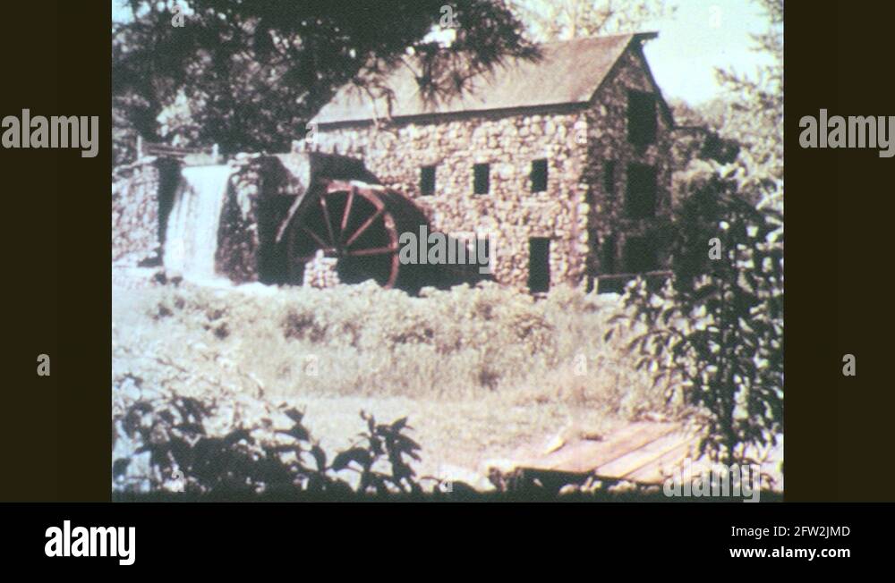 1950s: Stone mill house in woods. Mill wheel turns with falling water ...