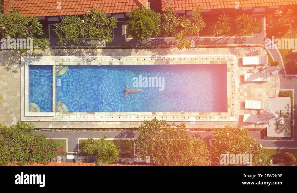 AERIAL LENS FLARE: Girl in pink bikini jumping and swimming in empty ...