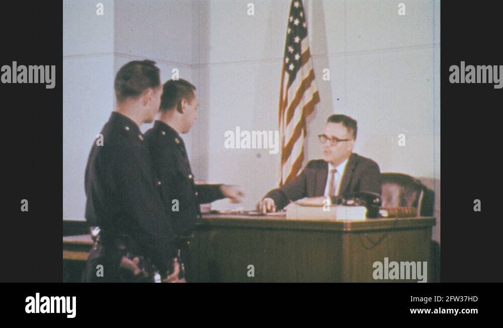 1960s: Judge sits behind desk, signs paper and hands to police officers ...