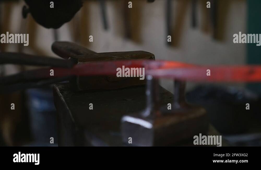 blacksmith working with hot glowing metal, bending steel in a smithery ...