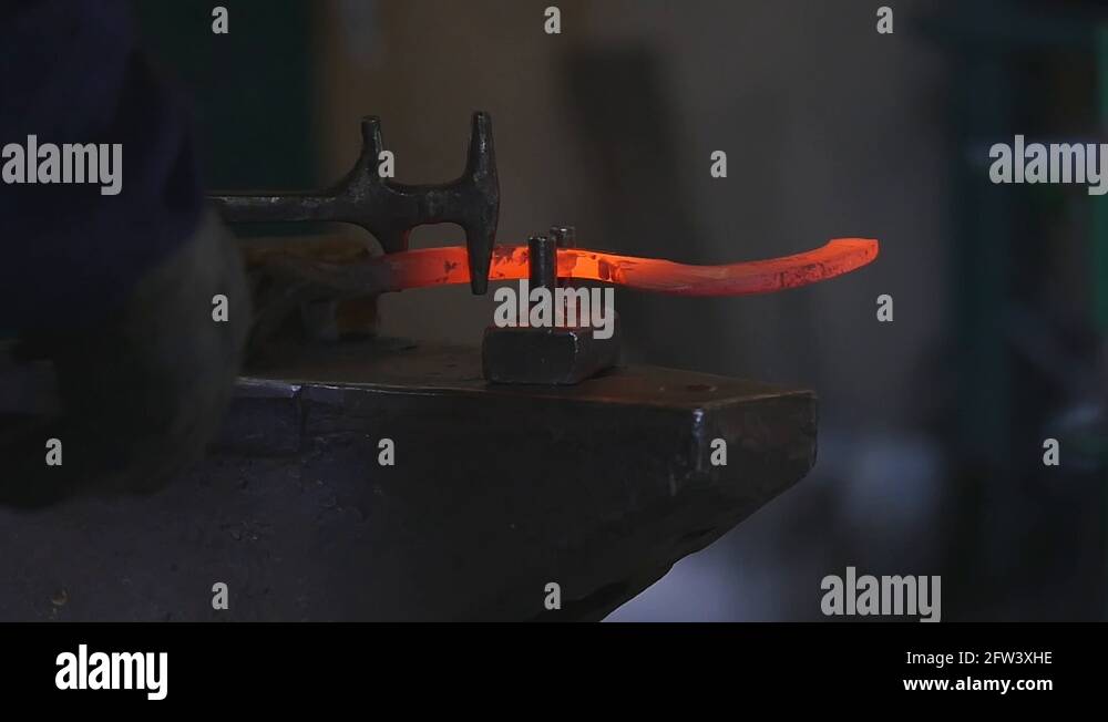 blacksmith working with hot glowing metal, bending steel in a smithery ...